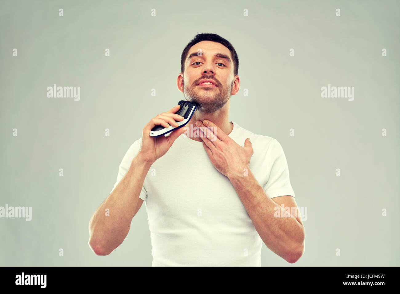 smiling man shaving beard with trimmer over gray Stock Photo - Alamy