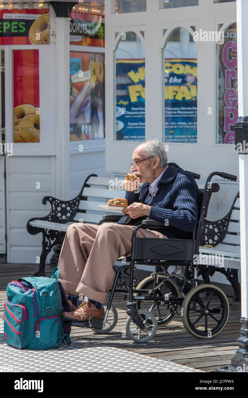 Elderly man sitting in a wheelchair eating a sandwich on Brighton ...