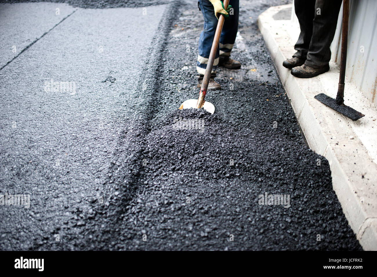 worker with shovel doing manual labor at road construction with asphalt ...