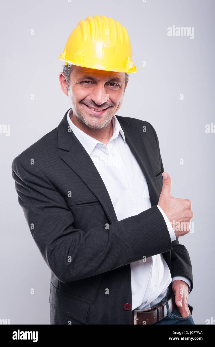 Foreman wearing hardhat making thumb up gesture and smiling on grey ...