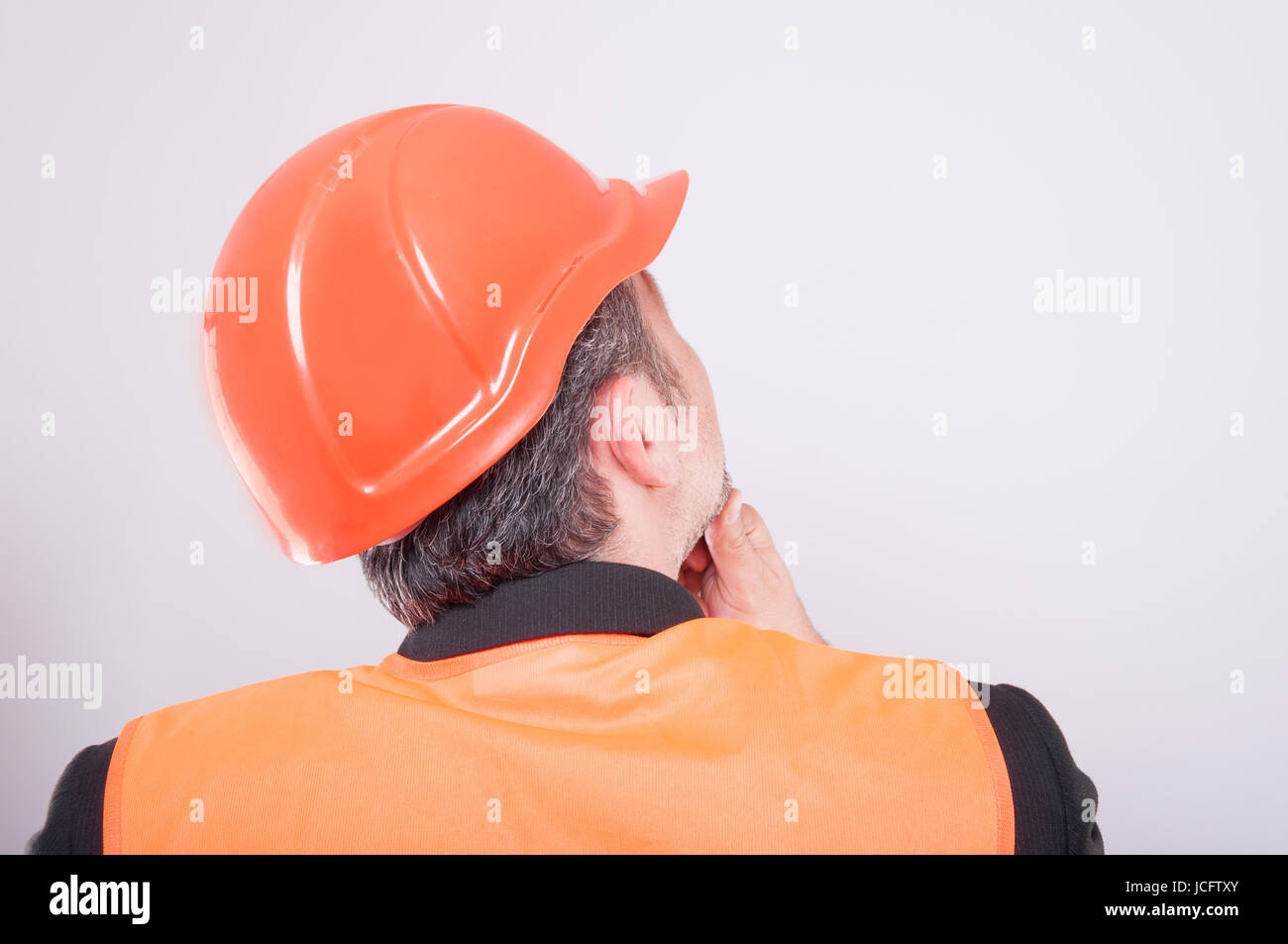 Back view of engineer making thinking gesture wearing hardhat and reflective vest on grey ...