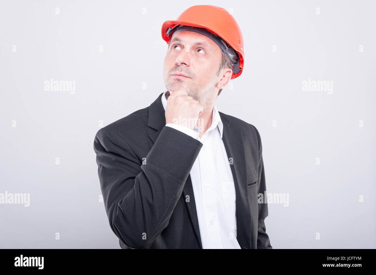 Engineer wearing hardhat making thinking gesture looking up on grey ...