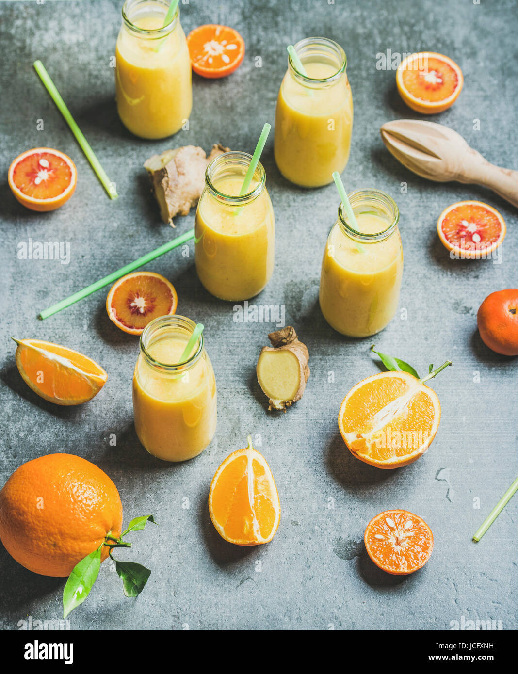 Healthy yellow smoothie with citrus fruit and ginger in bottles over ...