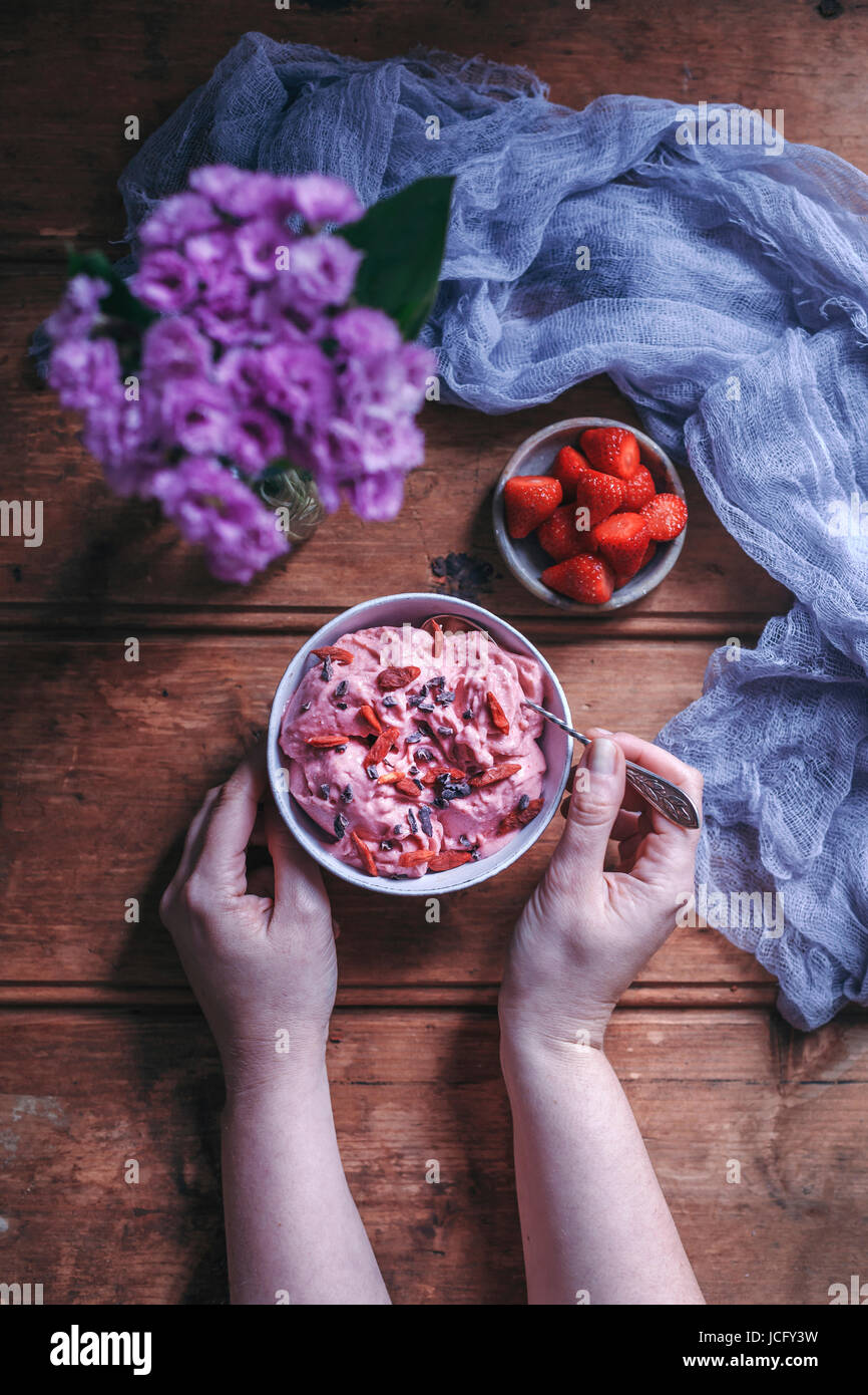 Woman eating strawberry banana ice cream in a bowl topped with goji ...