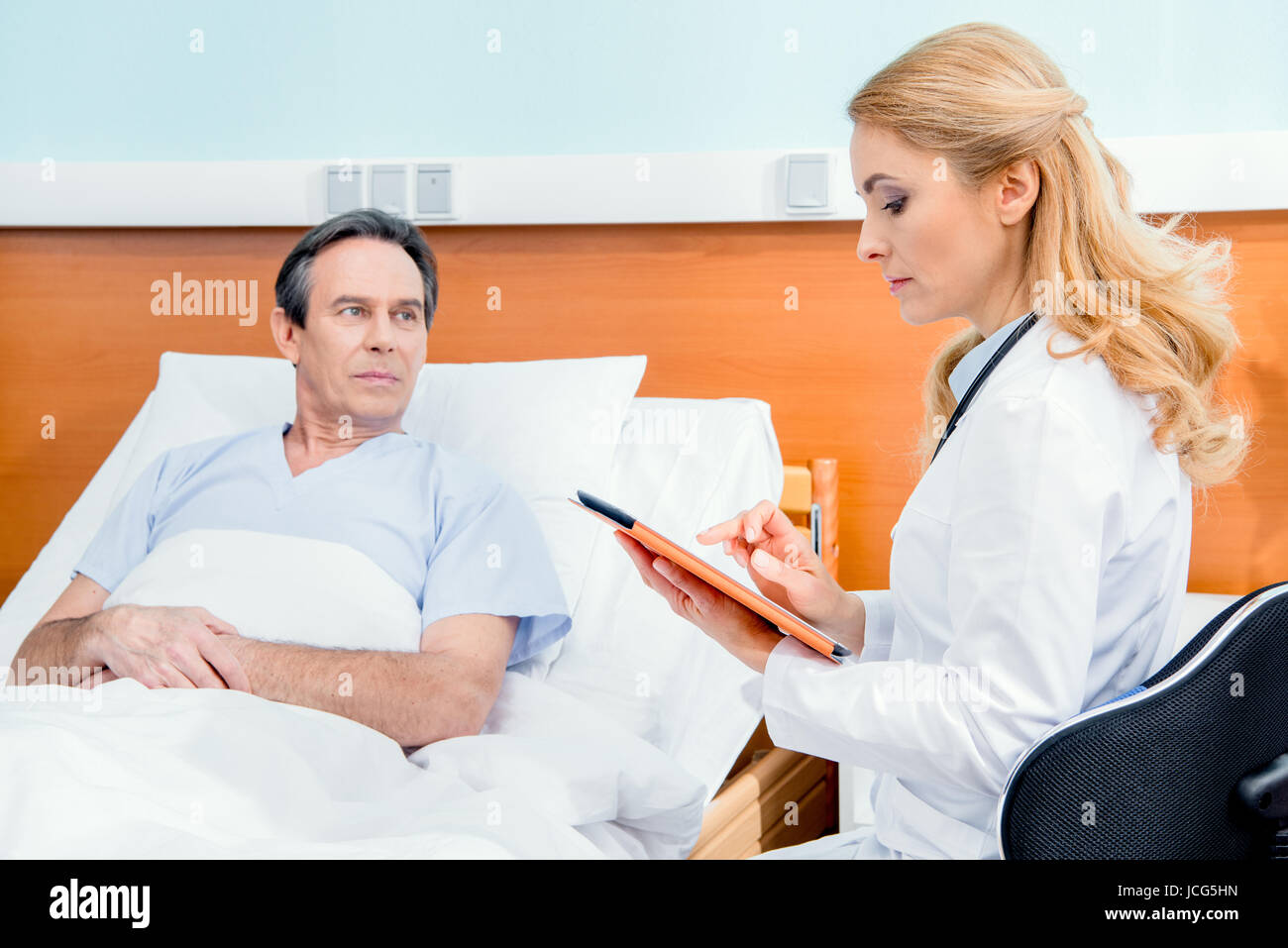 middle aged patient lying on bed, doctor using digital tablet and ...