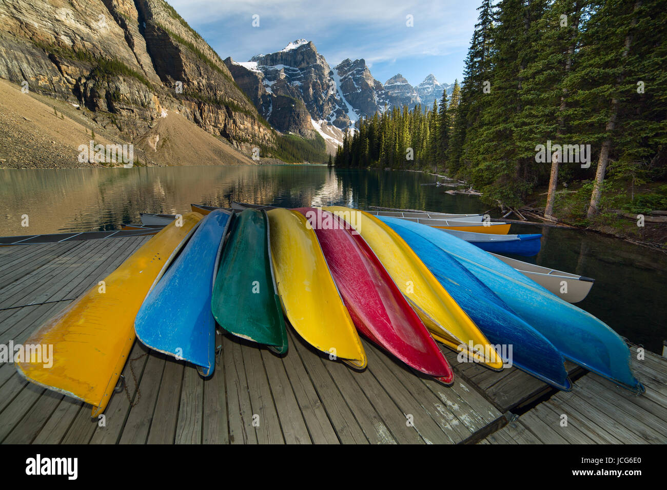 colorful canoes on wooden deck by a lake with mountain cliffs in the ...