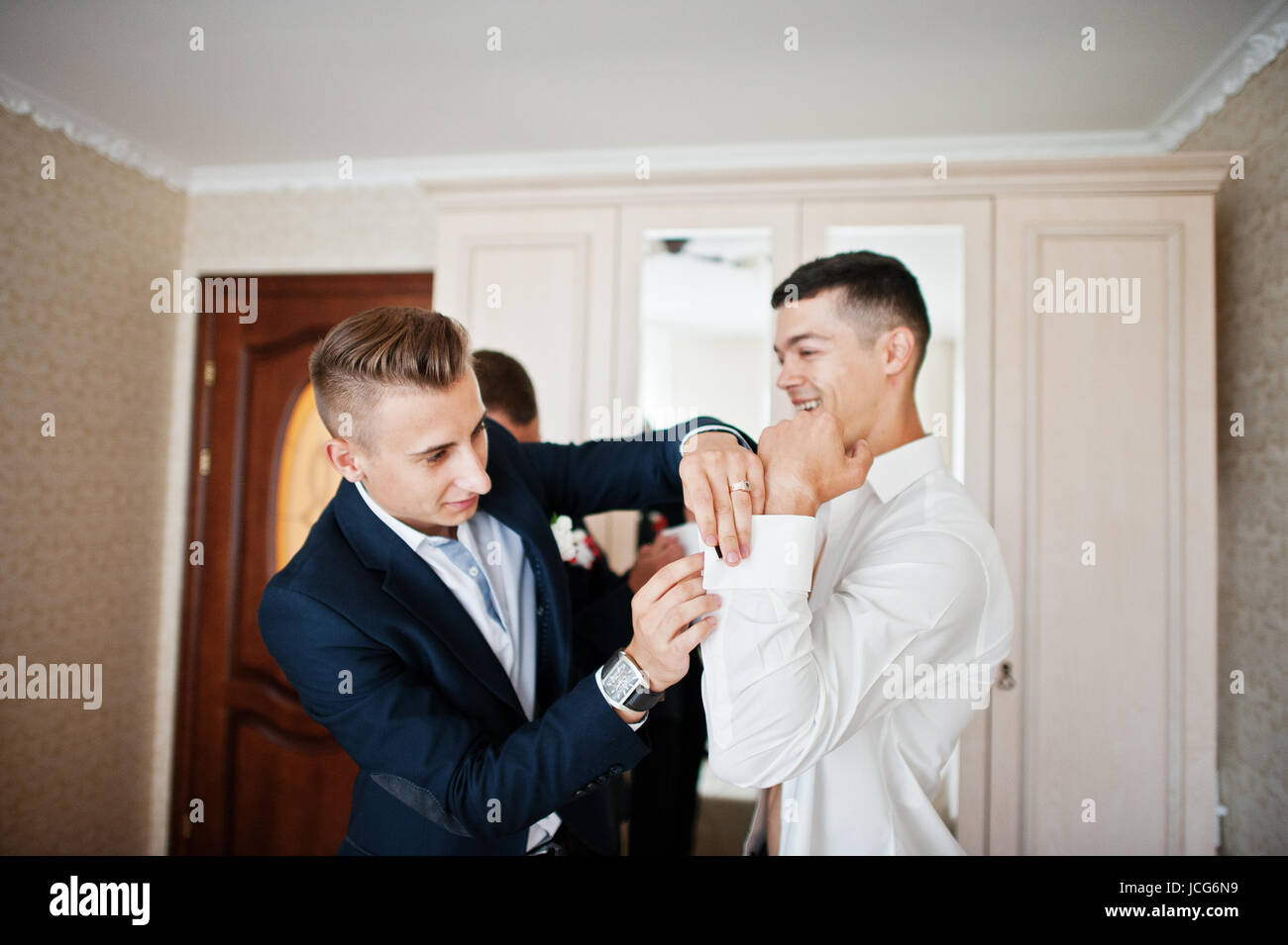 Groomsmen helping groom to dress up and get ready for his wedding in a ...