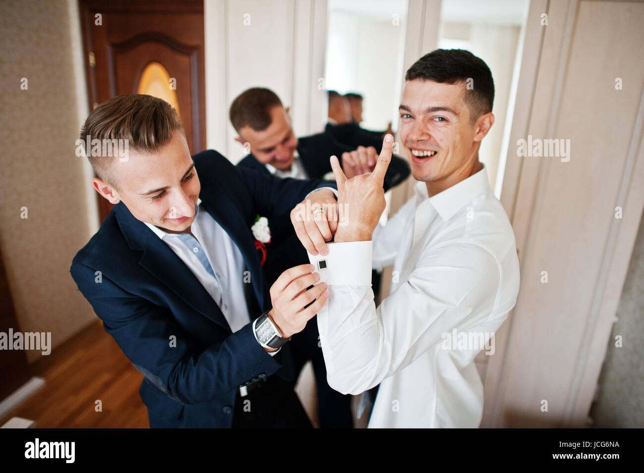 Groomsmen helping groom to dress up and get ready for his wedding in a ...