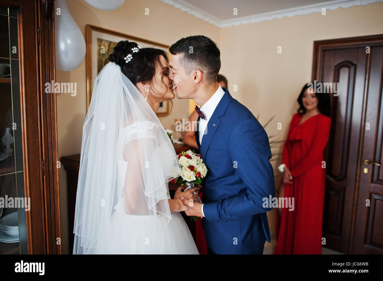 Wedding couple kissing in the room with bridesmaids in the background ...