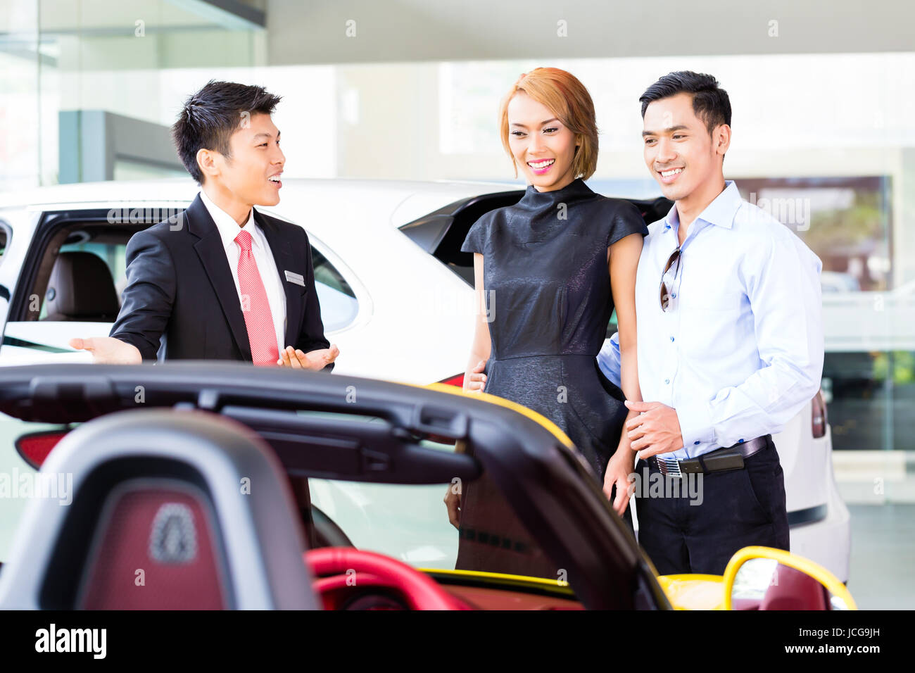 Asian couple buying car in auto dealership consulting the salesman ...