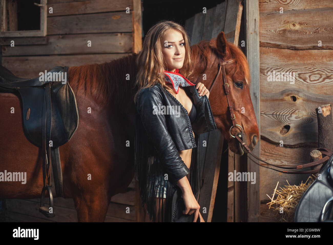 Beautiful girl in a leather jacket near the stables next to the horse ...