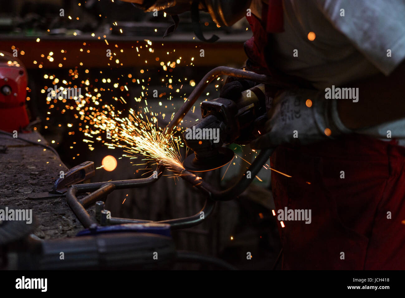 Worker using an electric grinder on steel structure in a workshop with ...