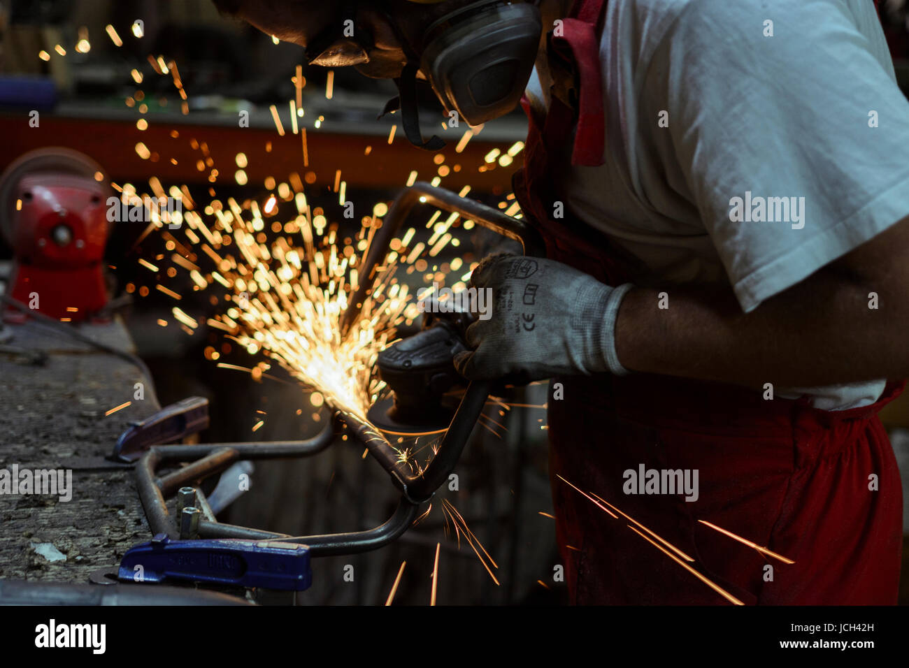 Worker using an electric grinder on steel structure in a workshop with ...