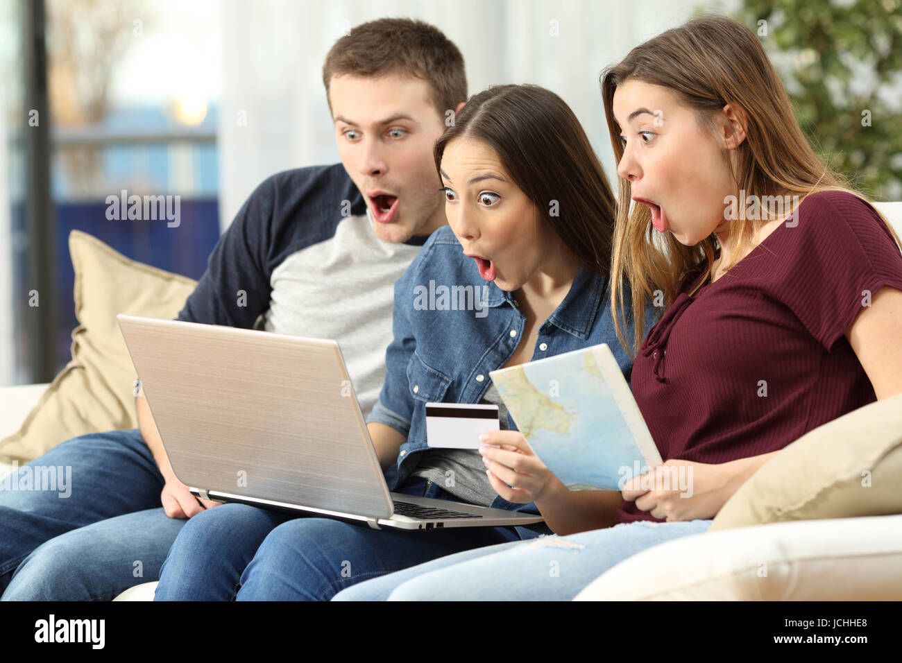 Three amazed friends finding trip offers on line with a laptop sitting ...