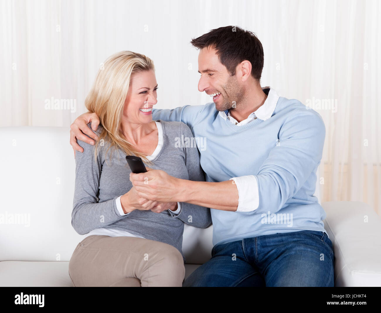 Young couple fighting for TV remote at home Stock Photo - Alamy