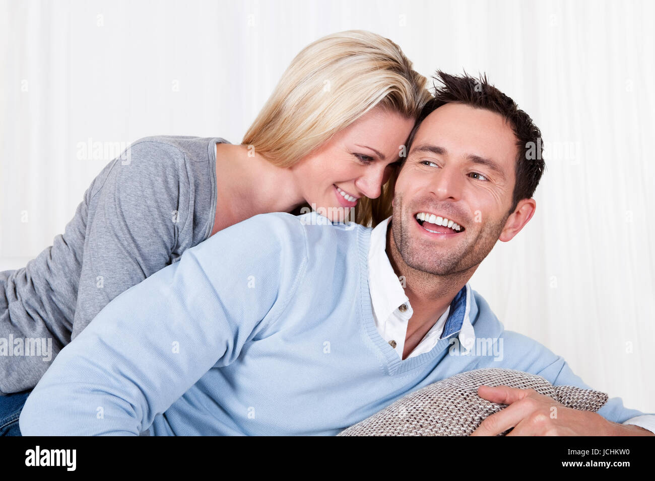 Happy attractive young man and woman smiling and cuddling as he relaxes ...