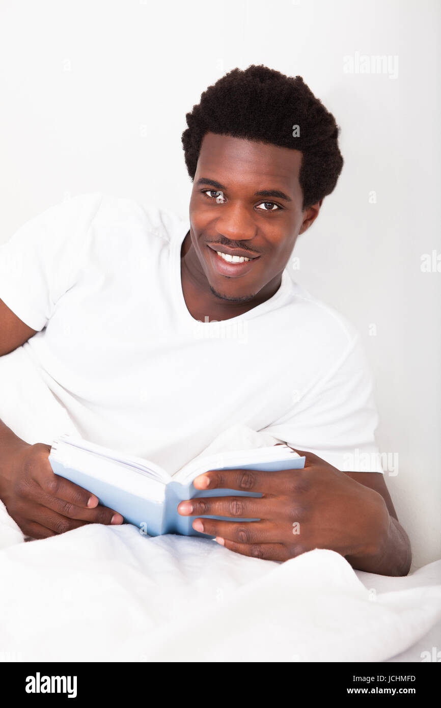 Happy Young African Man Reading His Book On Bed Stock Photo - Alamy