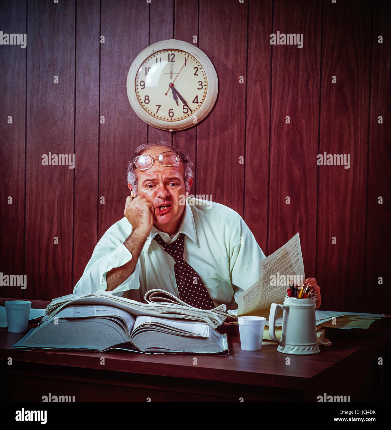 Exasperated, frustrated, overworked amid pikes of paperwork on desk ...