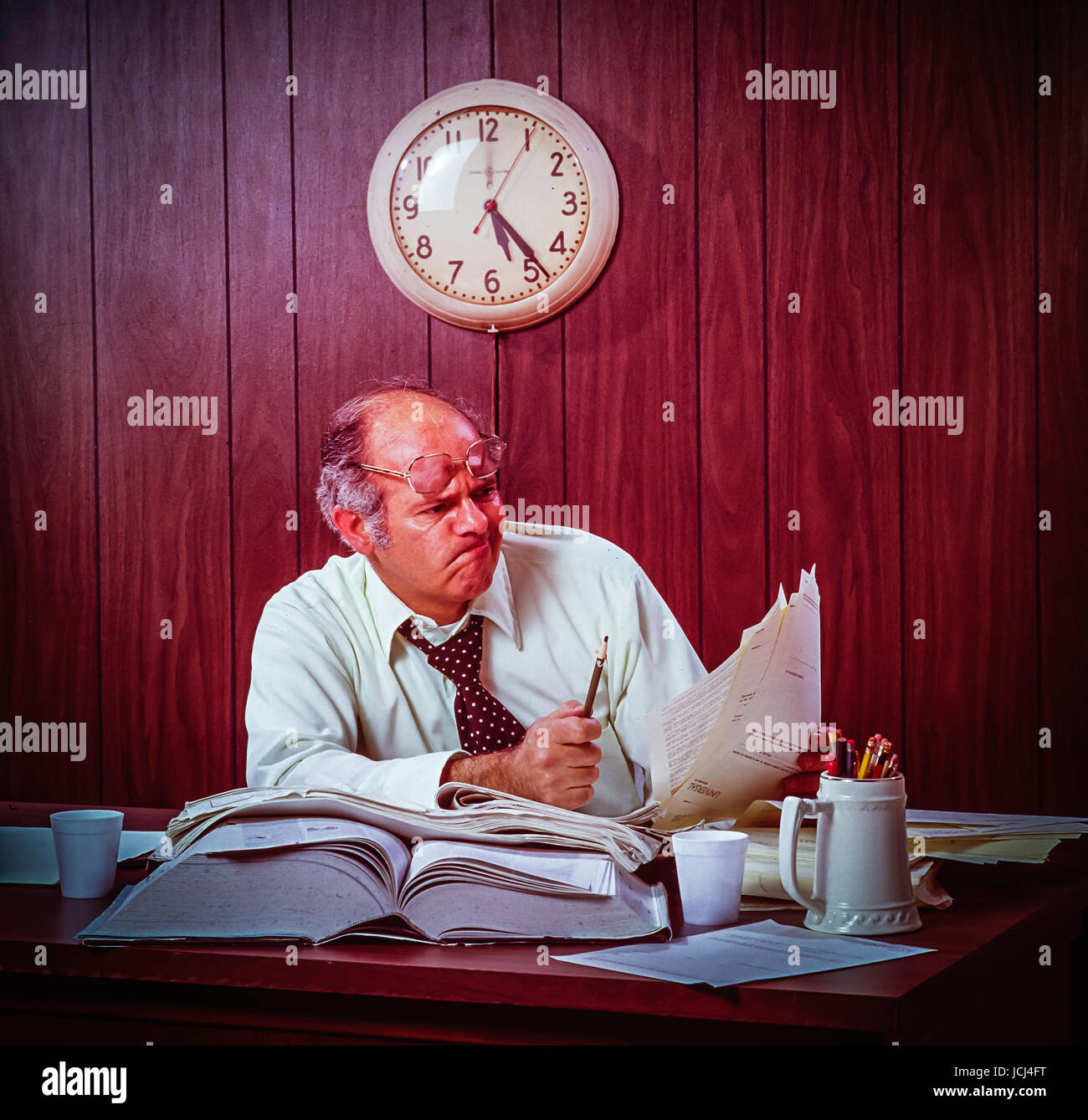 Exasperated, frustrated, overworked amid pikes of paperwork on desk ...