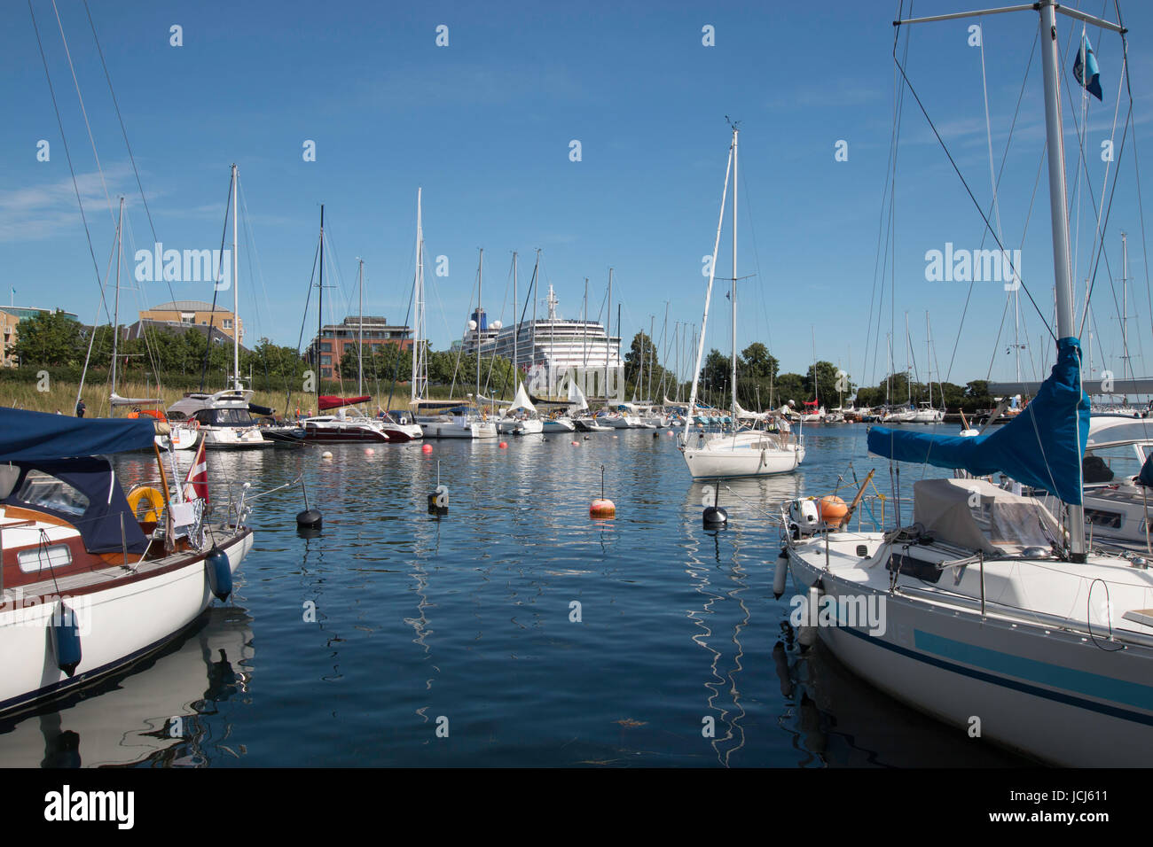 Two sailors aboard a yacht about to berth in a marina between two other ...