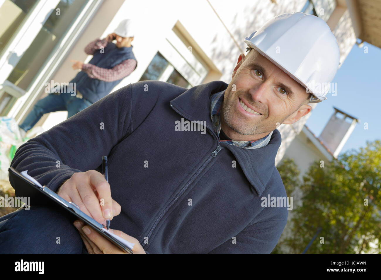 happy confident builder writing and using clipboard Stock Photo - Alamy