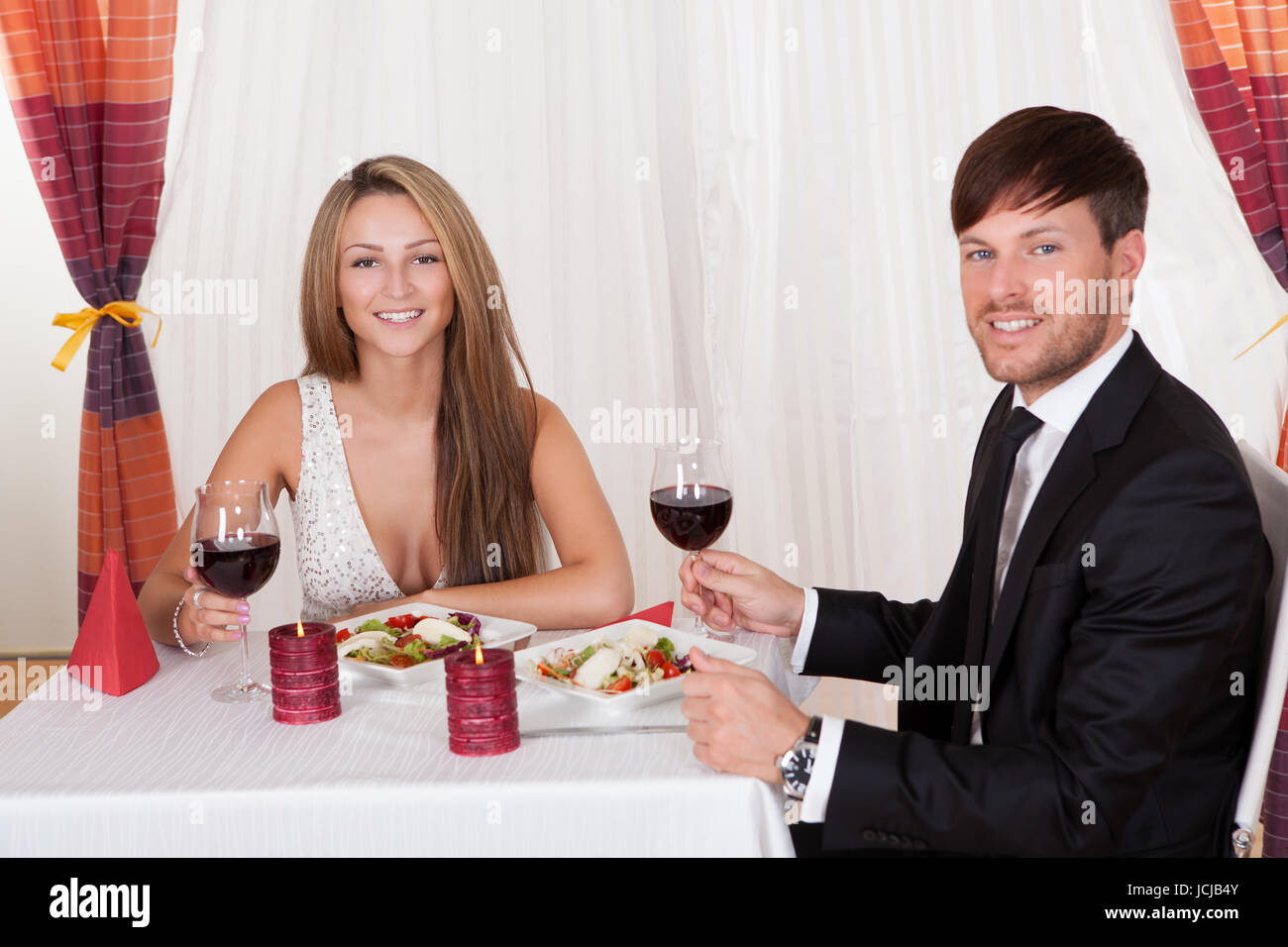 Young couple seated at a restaurant table enjoying a romantic dinner by ...