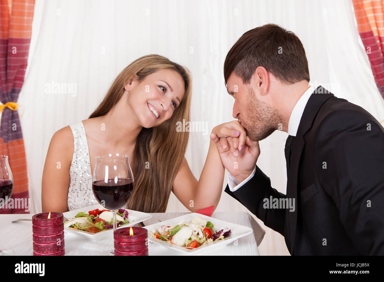 Man kissing a woman's hand at a romantic dinner as she looks at him ...
