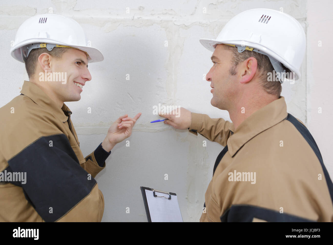 builder and colleague in uniform pointing at white wall Stock Photo - Alamy