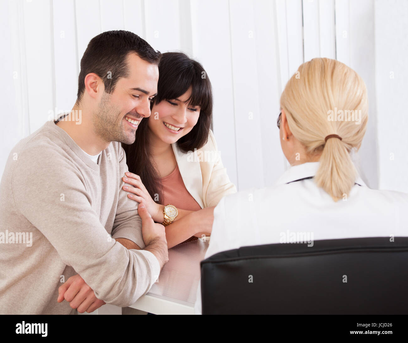 Happy Doctor Discussing With Couple In Clinic Stock Photo - Alamy