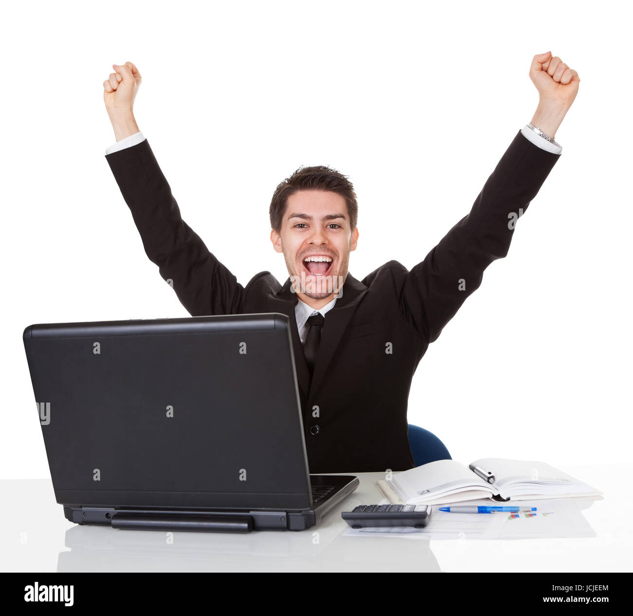 Businessman sitting at his desk rejoicing throwing his arms up in the ...