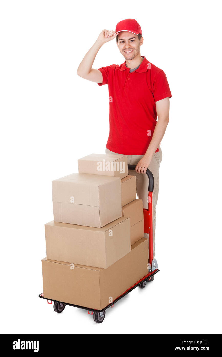 Cheerful young deliveryman in a red uniform holding trolley loaded with ...