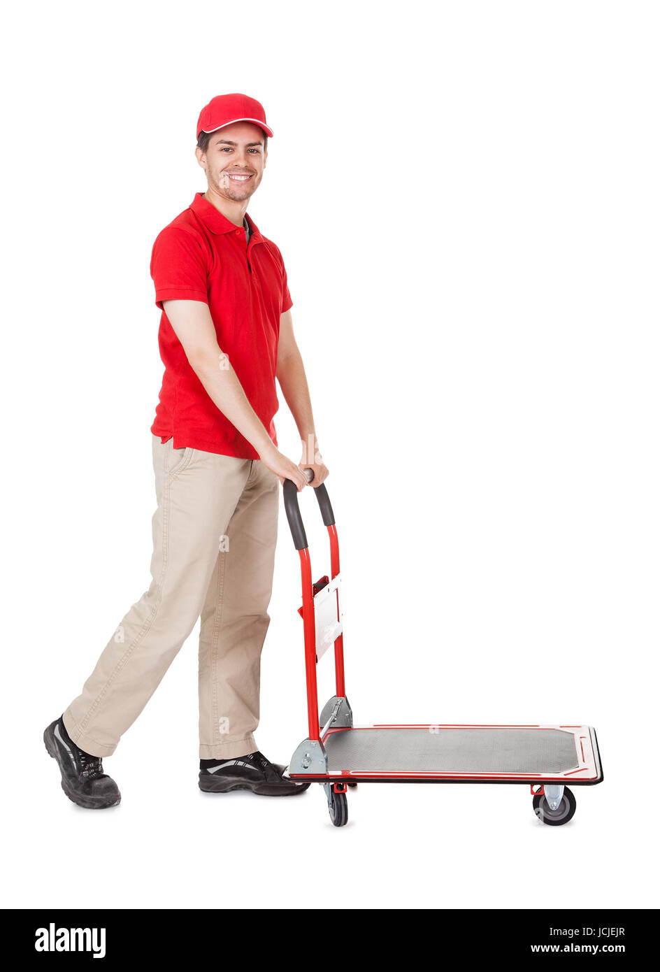 Cheerful young deliveryman in a red uniform holding trolley loaded with ...