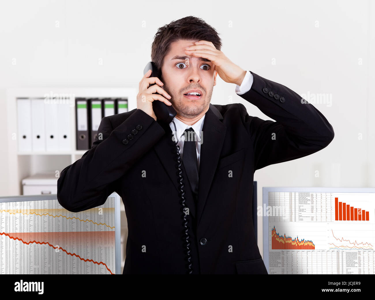 Worried stock broker talking on the phone backed by graphs depicting a ...