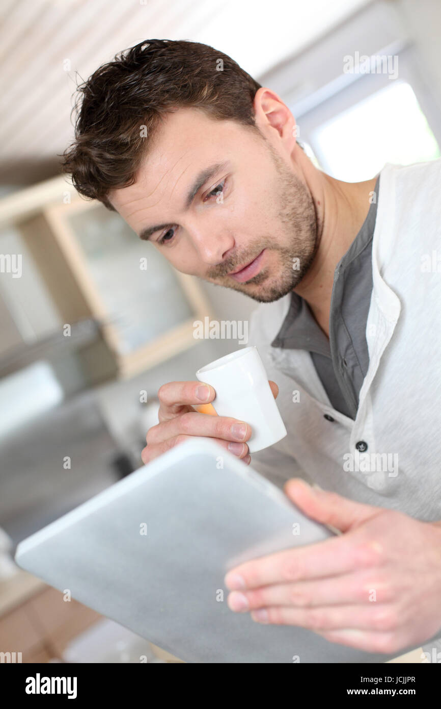 Young man using electronic tablet while drinking coffee Stock Photo - Alamy