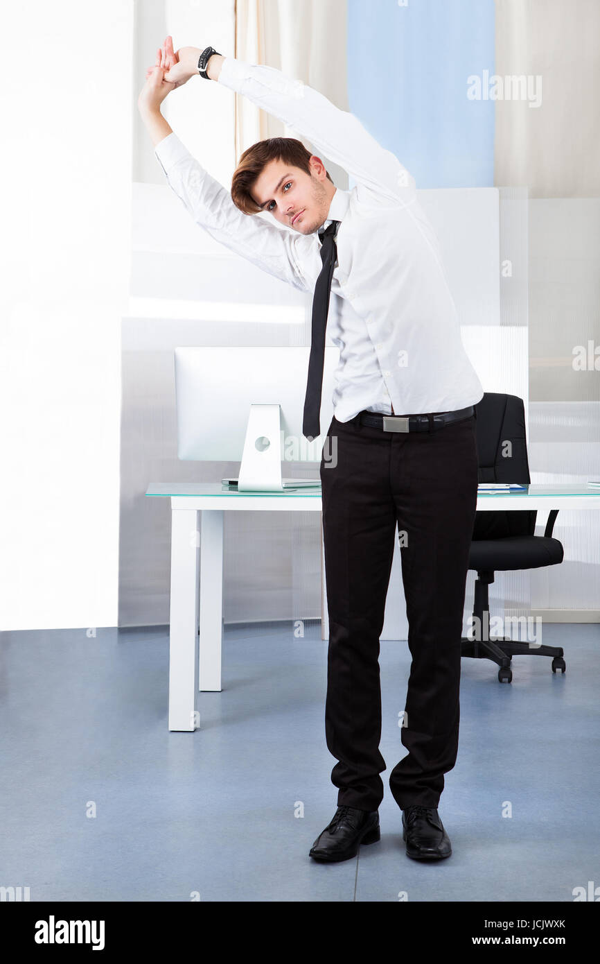 Portrait Of A Young Businessman Stretching In Office Stock Photo - Alamy