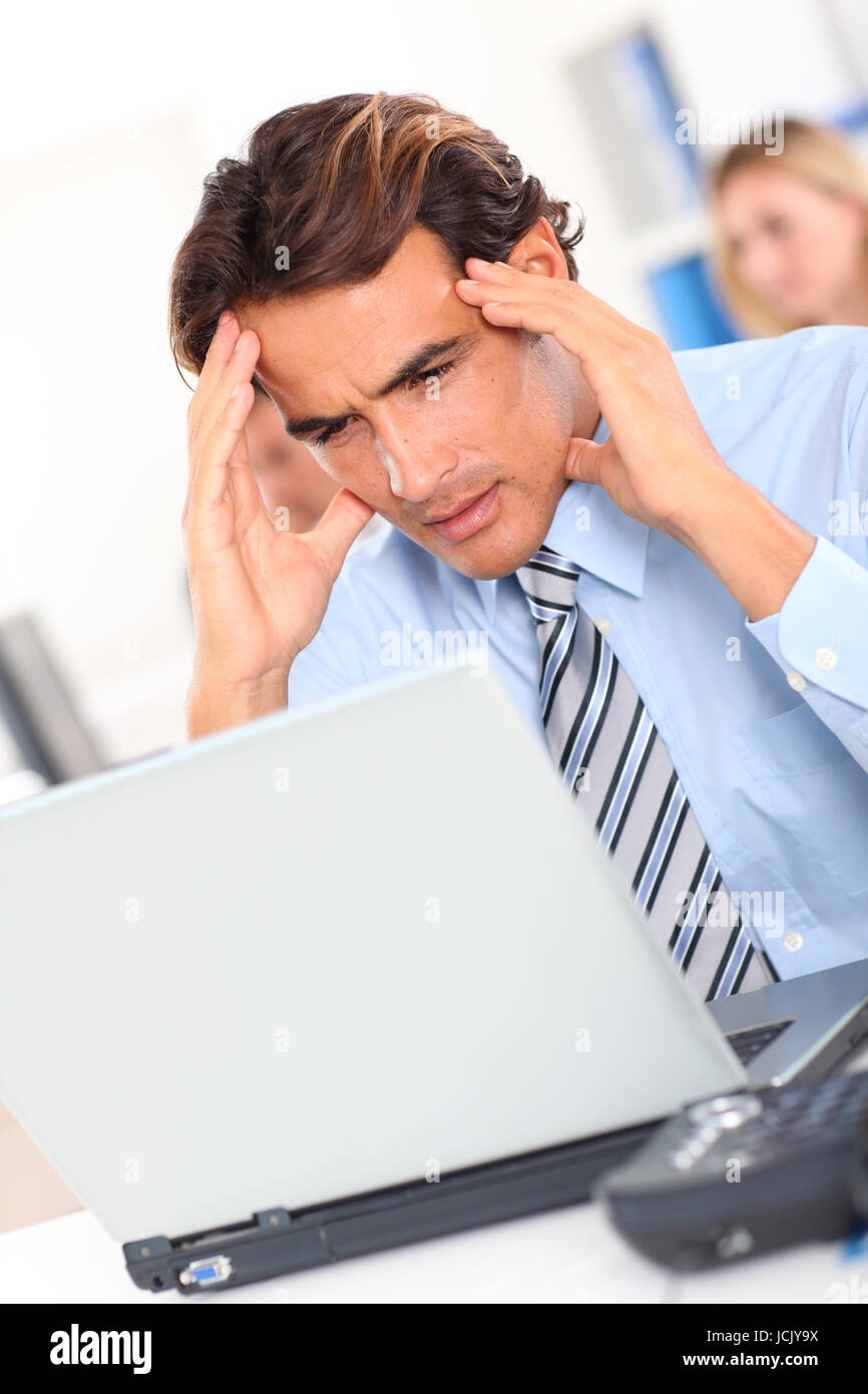 Businessman having a headache in front of laptop Stock Photo - Alamy