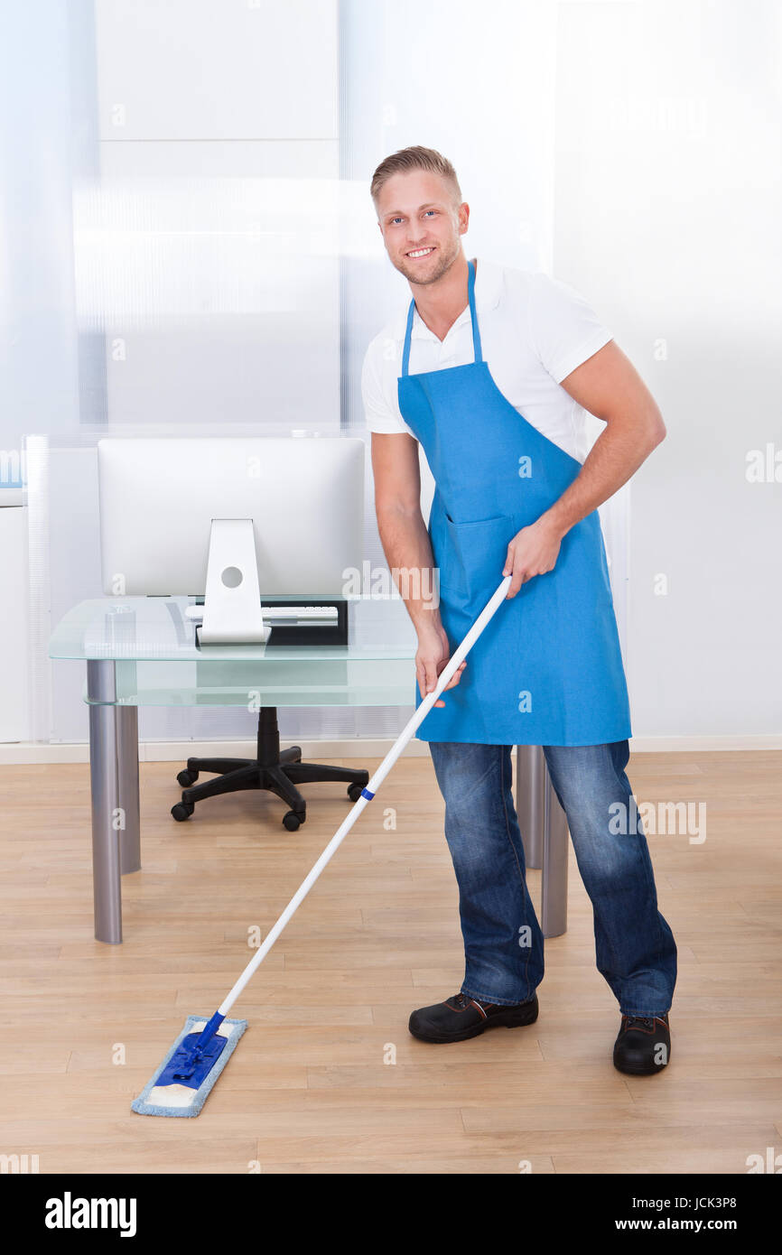 Handsome male janitor or cleaner cleaning the floor in an office ...