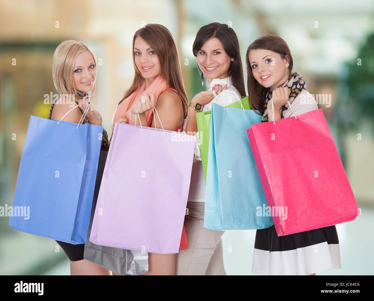 Four happy beautiful female shoppers carrying colorful shopping bags ...