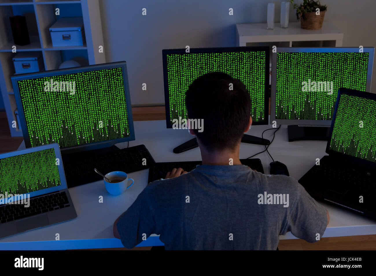 Rear high angle view of a male hacker sitting at a desk surrounded by ...