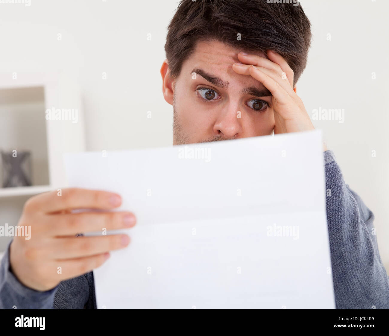 Horrified young man reading a document with an aghast expression and ...