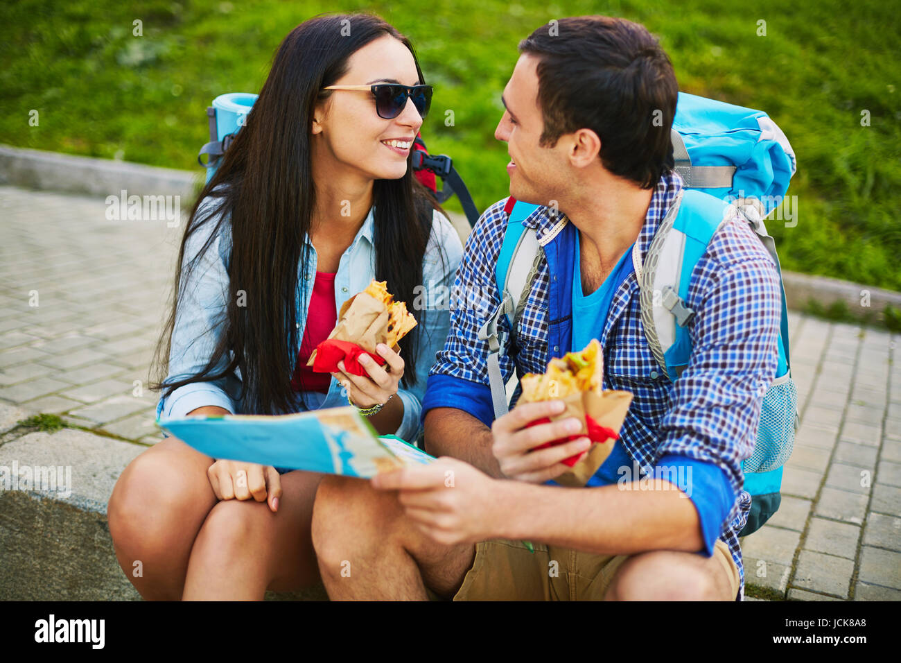 Happy travelers smiling on one another while sitting on pavement and ...