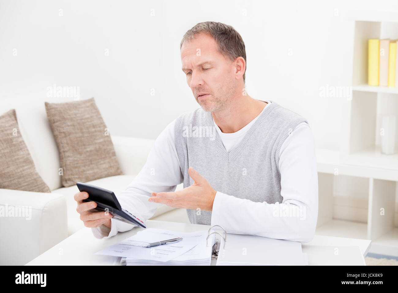 Portrait Of A Thoughtful Man Holding Calculator At Home Stock Photo - Alamy