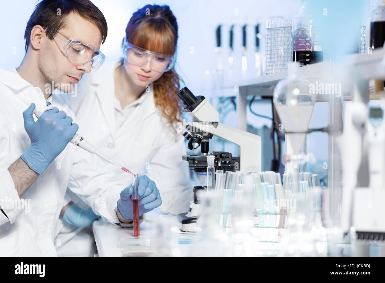 Young male researcher pipetting red liquid in the glass tube in the ...