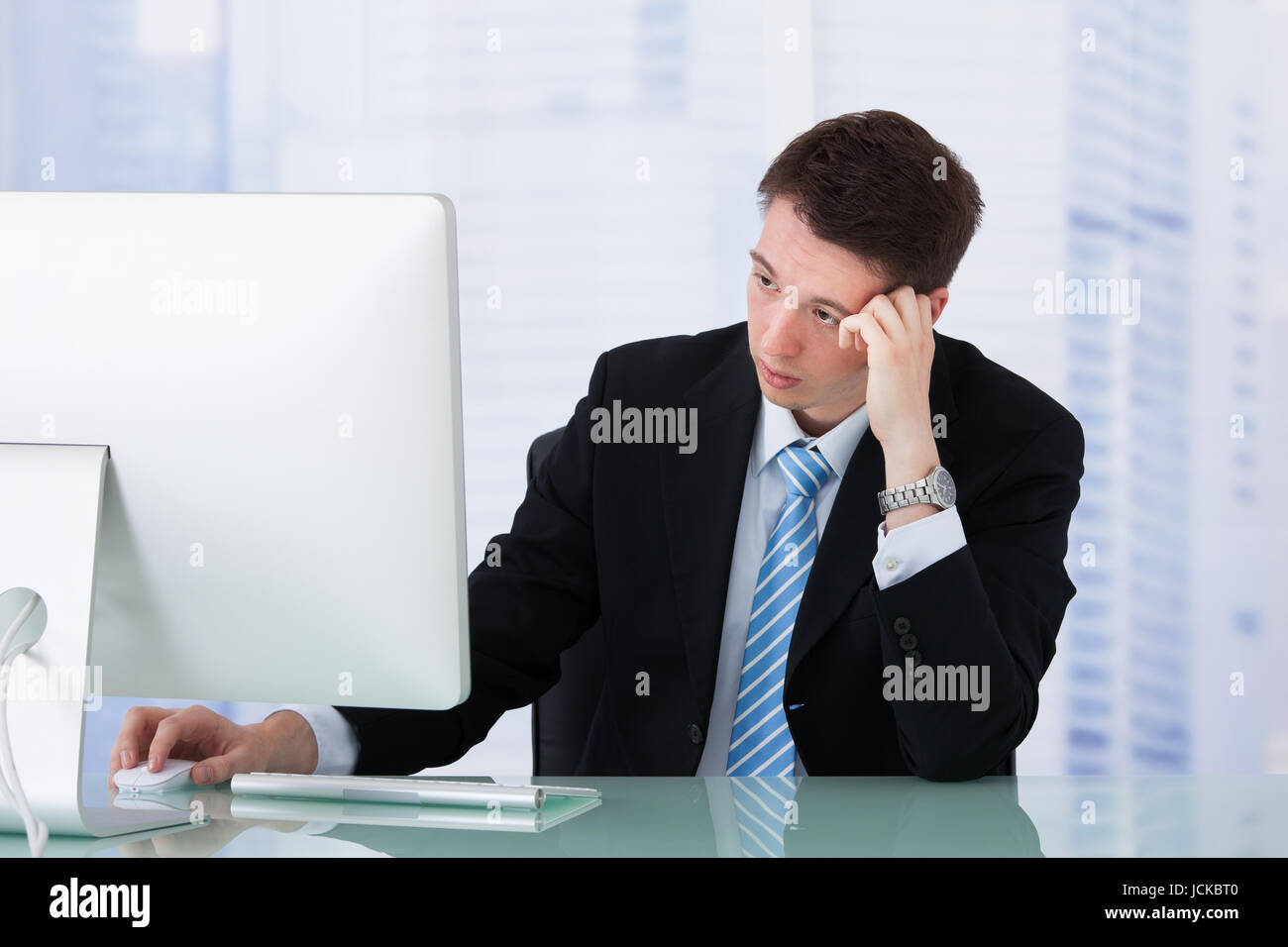 Worried young businessman looking at computer at office desk Stock ...