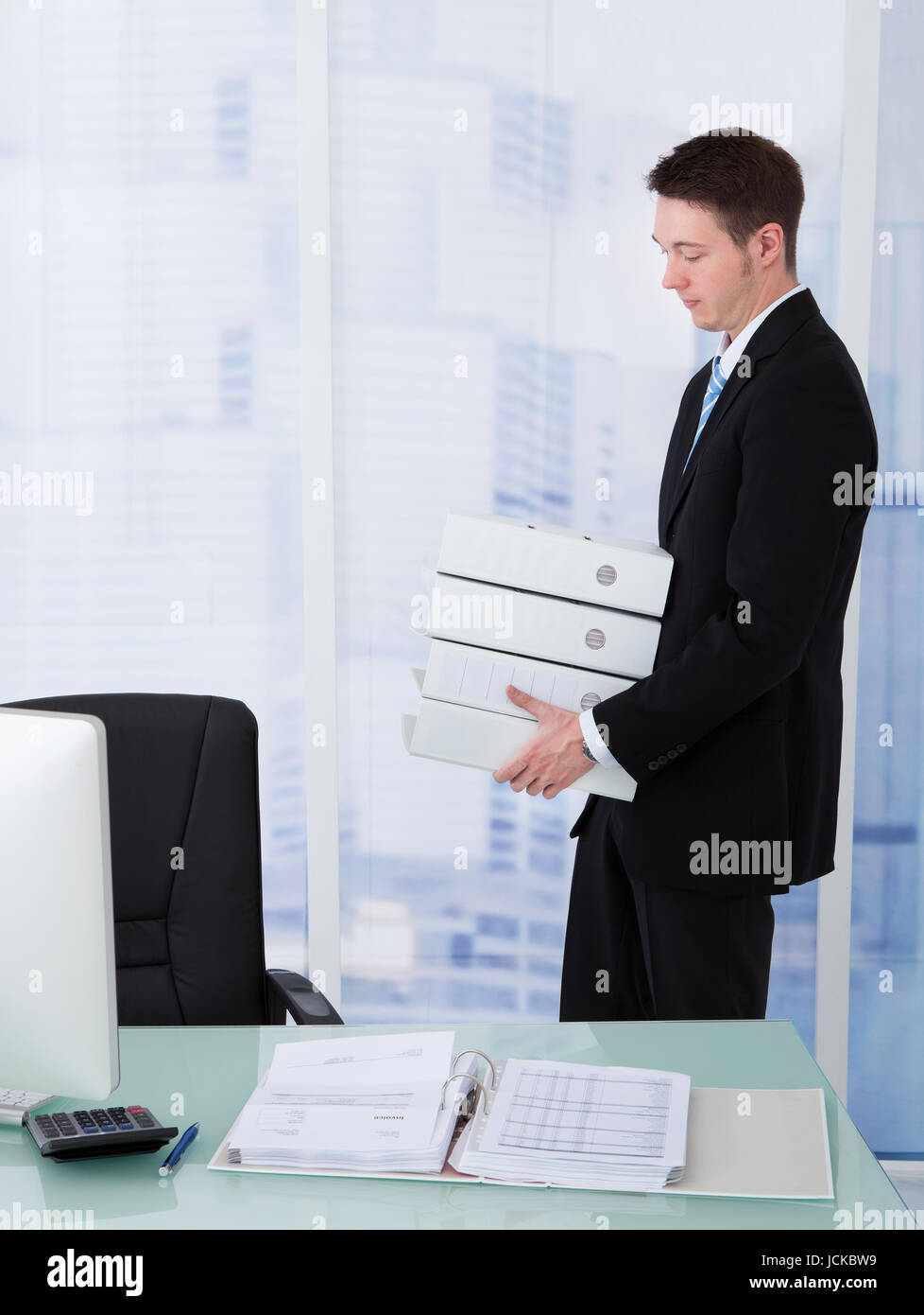 Side view of young businessman carrying stacked binders at office desk ...