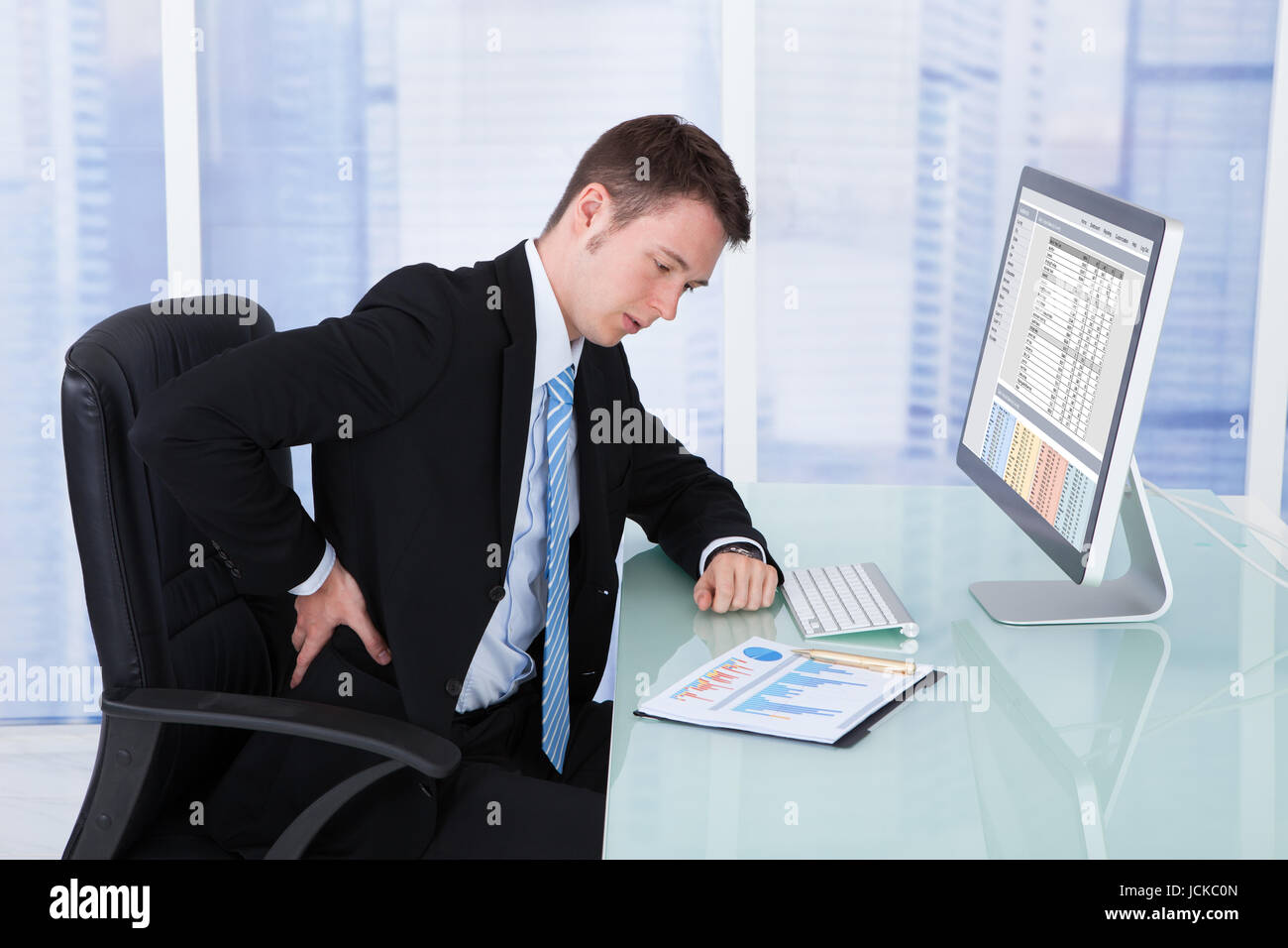 Young businessman suffering from backache at computer desk in office ...