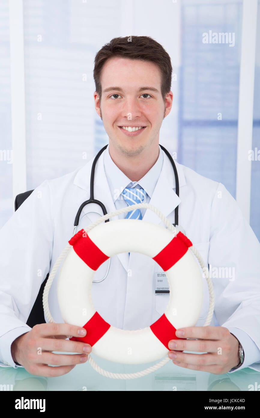 Portrait of confident young male doctor holding lifebuoy in clinic ...