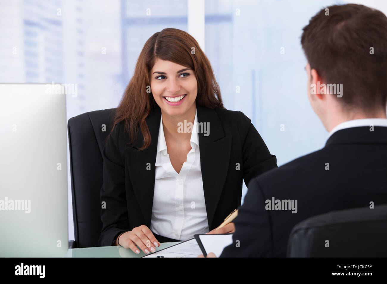Happy young businesswoman interviewing male candidate at desk in office ...