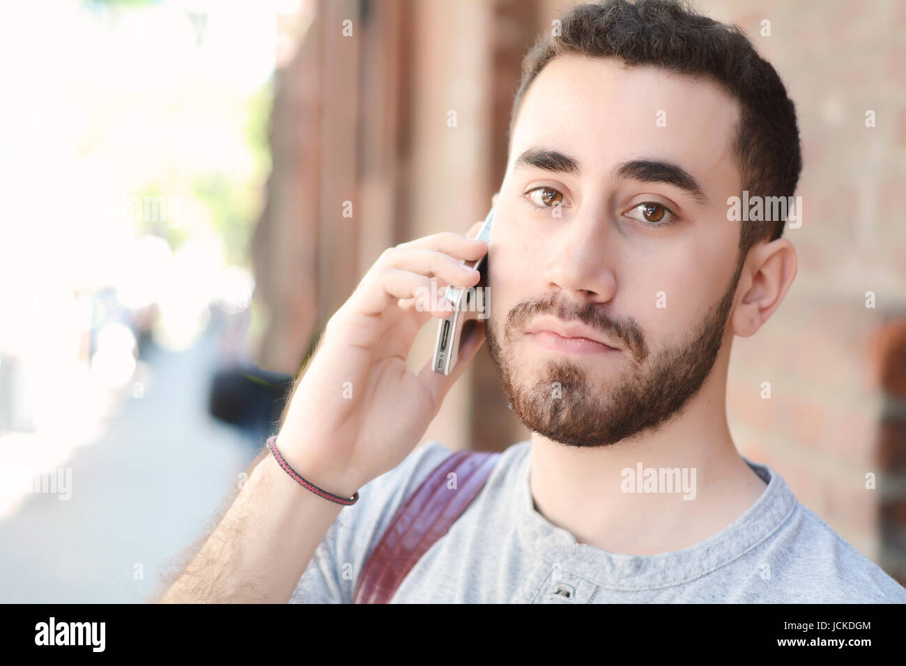 Portrait of young latin man talking on the phone against brick wall ...