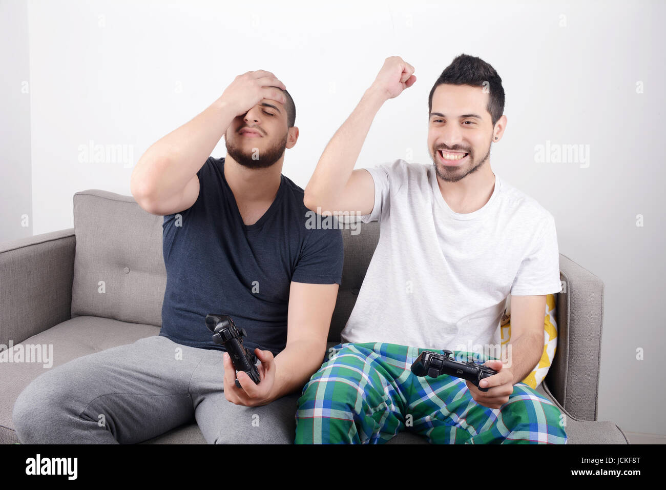 Portrait of two friends playing videogames and sitting on couch ...
